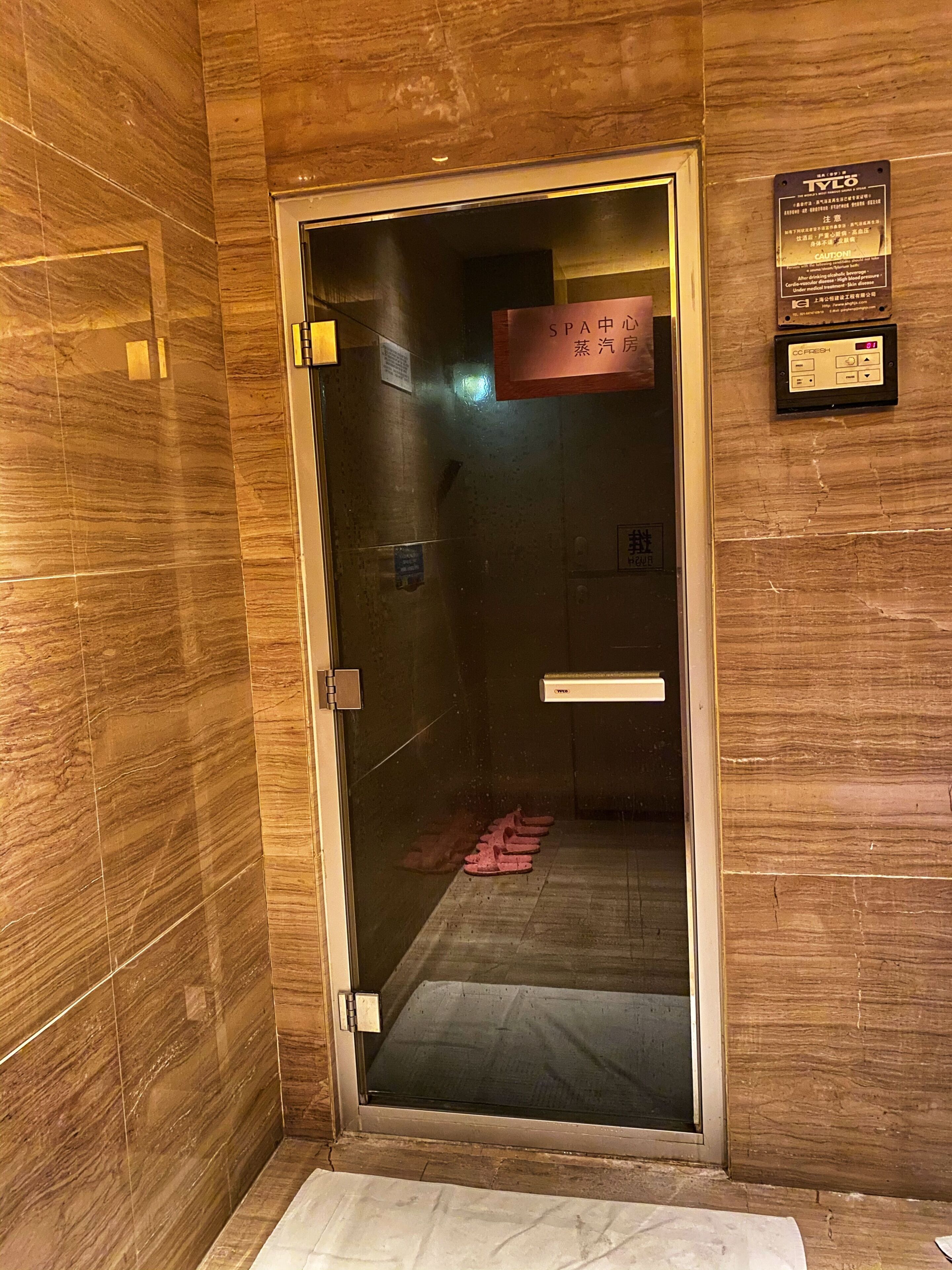 Entrada de um spa, com porta de vidro, placa indicando centro de spa e porta-toalhas com toalhas.