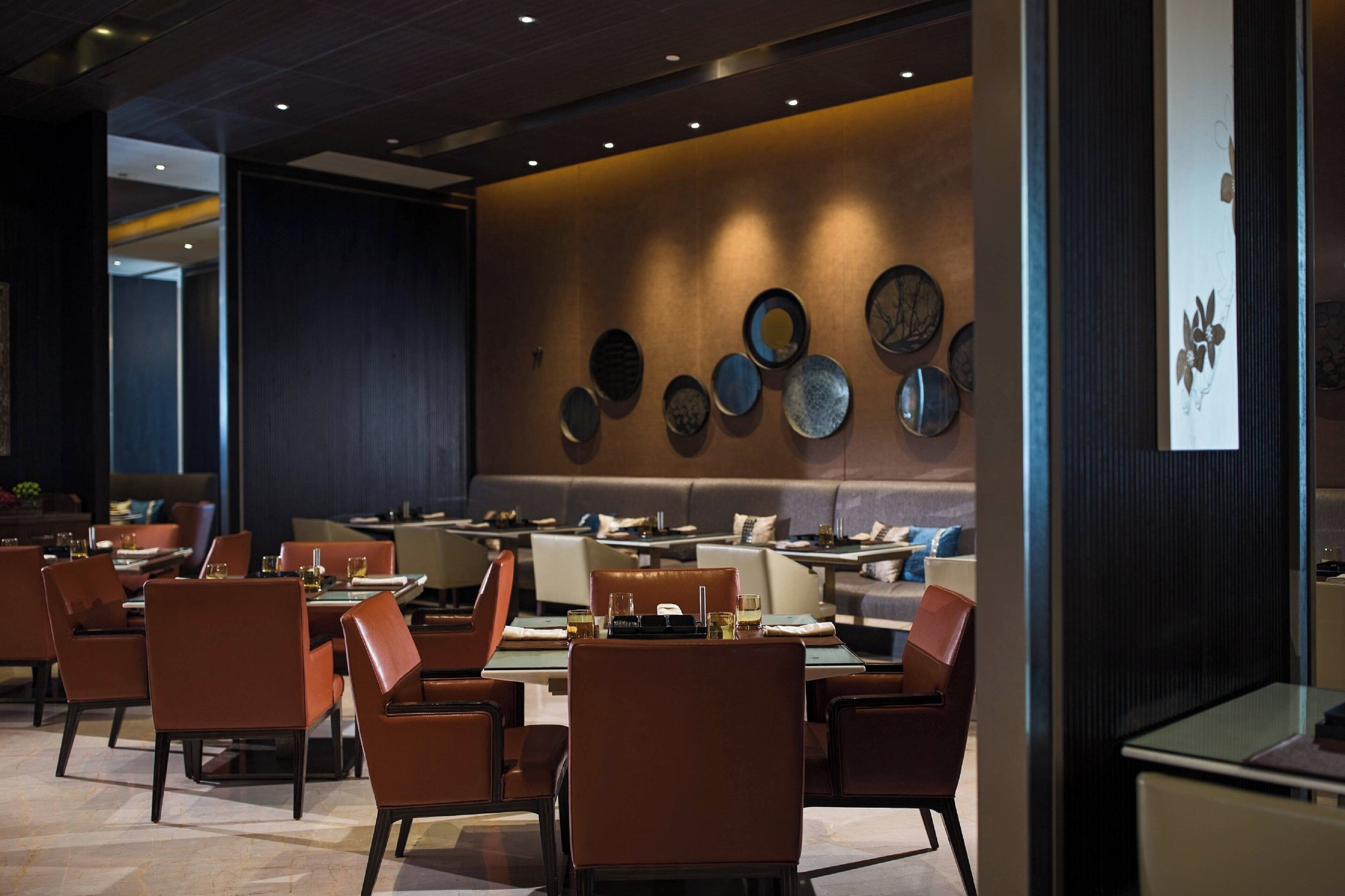 Restaurante moderno com várias mesas e cadeiras, parede decorada com pratos e um painel de madeira escura à direita.