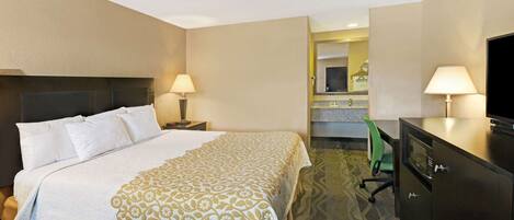 Quarto de hotel com cama, duas luminárias de cabeceira, escrivaninha com cadeira, televisão e micro-ondas.