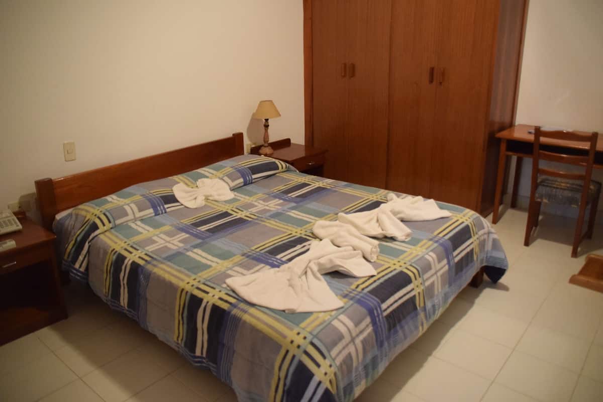 Quarto com cama, guarda-roupa de madeira, mesa de cabeceira e uma cadeira.