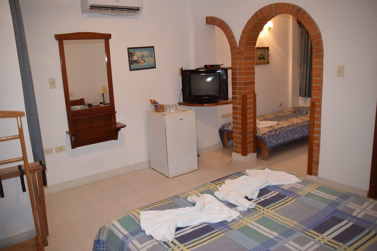 Quarto com cama, televisão, pequeno frigorífico, espelho e arco de tijolos.