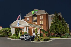 Edifício Holiday Inn Express com entrada coberta, uma bandeira e um estacionamento com carros.