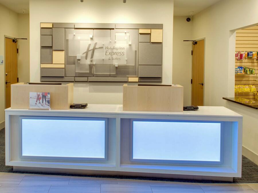 Balcão de recepção de hotel com design moderno, apresentando uma grande placa iluminada acima e uma pequena vitrine com folhetos.