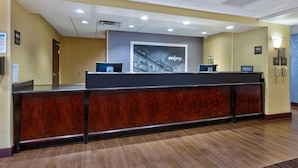 Uma receção de hotel com acabamento em madeira, um ecrã digital e um cartaz grande na parede.