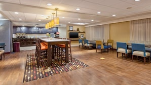 Um saguão de hotel com área de refeições, cozinha e espaço de estar com televisão e obras de arte.