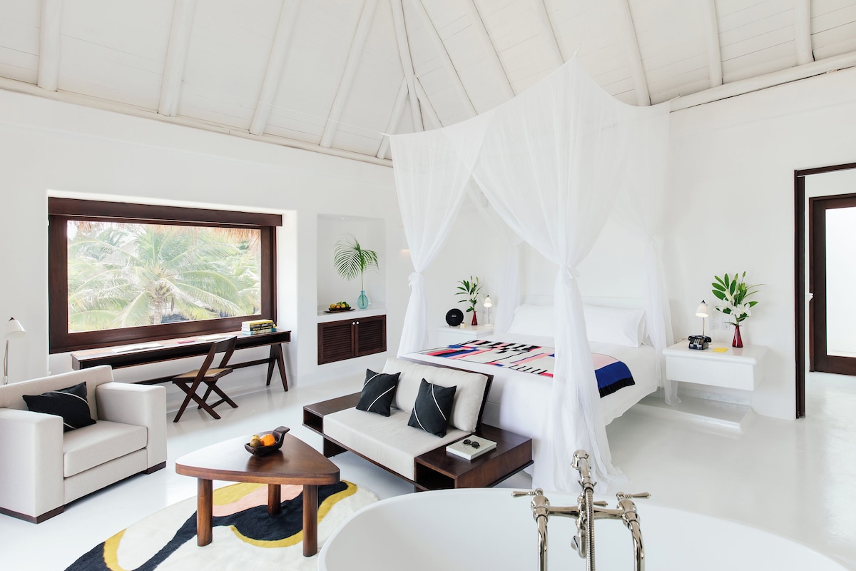 Quarto moderno com cama sob dossel, sofá, escrivaninha e janela grande.