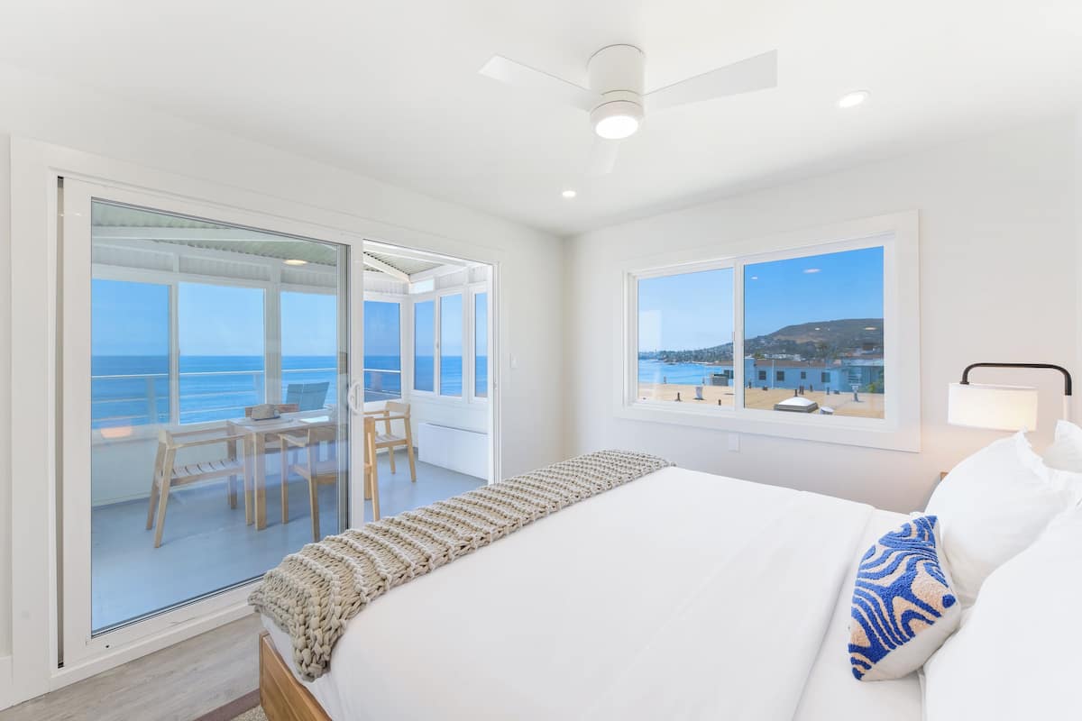 Quarto com uma cama grande, vista para o mar e varanda com mesa e cadeiras.