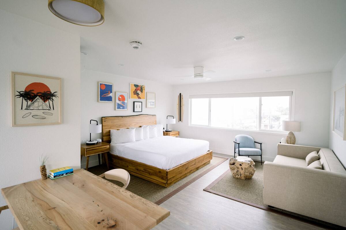 Quarto moderno com cama de madeira, escrivaninha, cadeira e sofá.