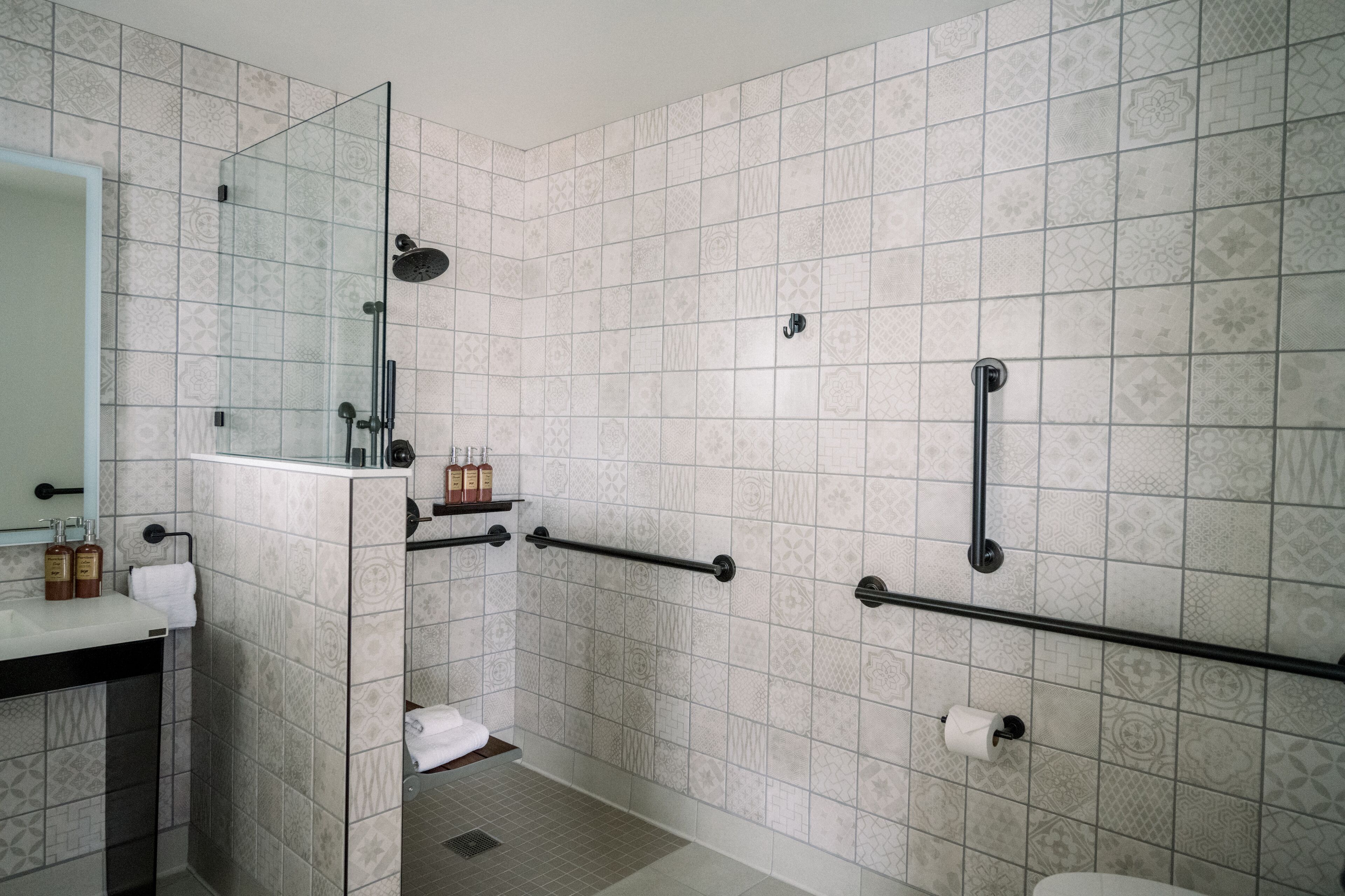 Um banheiro moderno com azulejos estampados, box de vidro, pia com artigos de higiene pessoal e vaso sanitário.