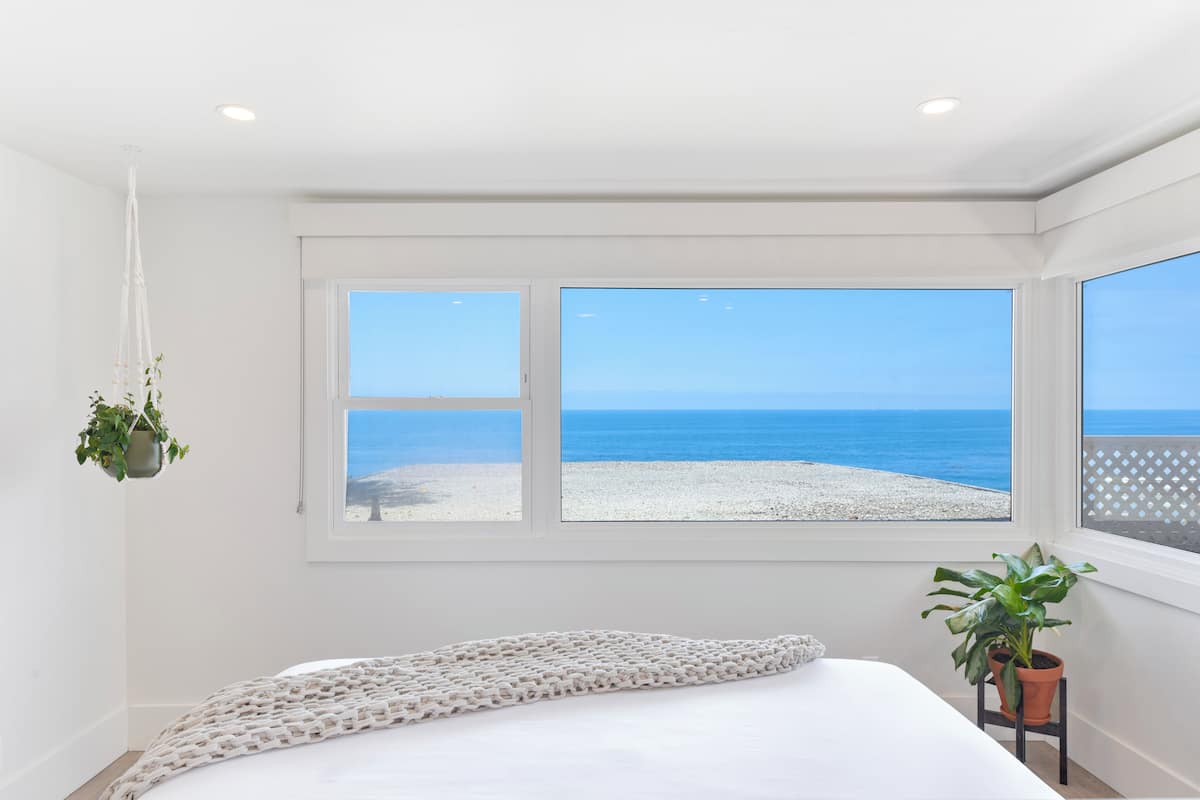 Quarto com uma grande janela que oferece vista para a praia e o mar.
