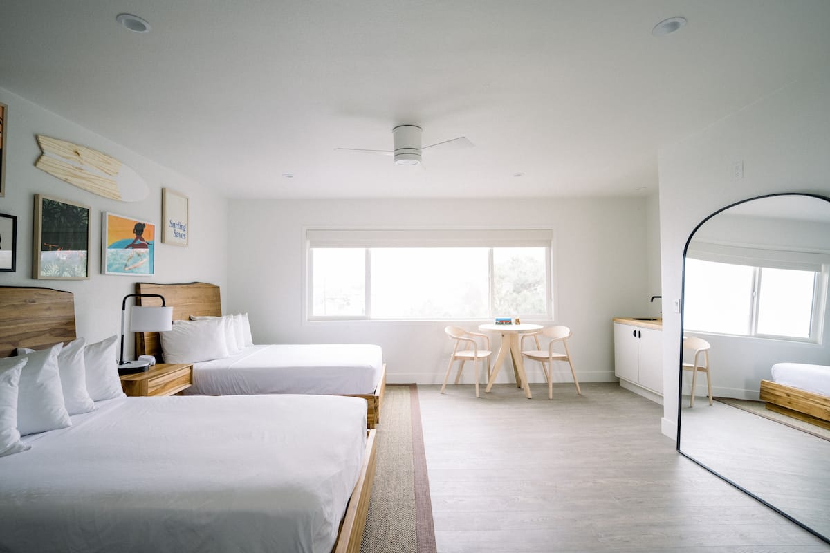 Quarto de hotel moderno com duas camas, uma pequena área de refeições e um espelho grande.