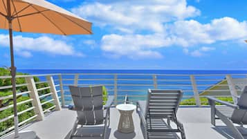 Terraço com cadeiras brancas, uma mesa e um guarda-sol com vista para a praia.