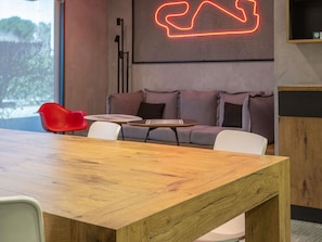 Um interior moderno com uma mesa de madeira, cadeiras vermelhas e brancas, um sofá cinzento e um letreiro de neon.