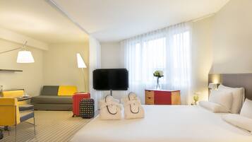 Quarto de hotel com cama, escrivaninha, cadeira, televisão e janela com cortinas.