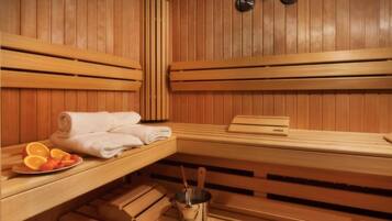 Uma sauna com bancos de madeira, um porta-toalhas e uma pequena mesa com frutas e um balde.
