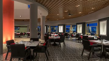 Um restaurante espaçoso com pé direito alto, piso estampado e grandes janelas com vista para a paisagem urbana.