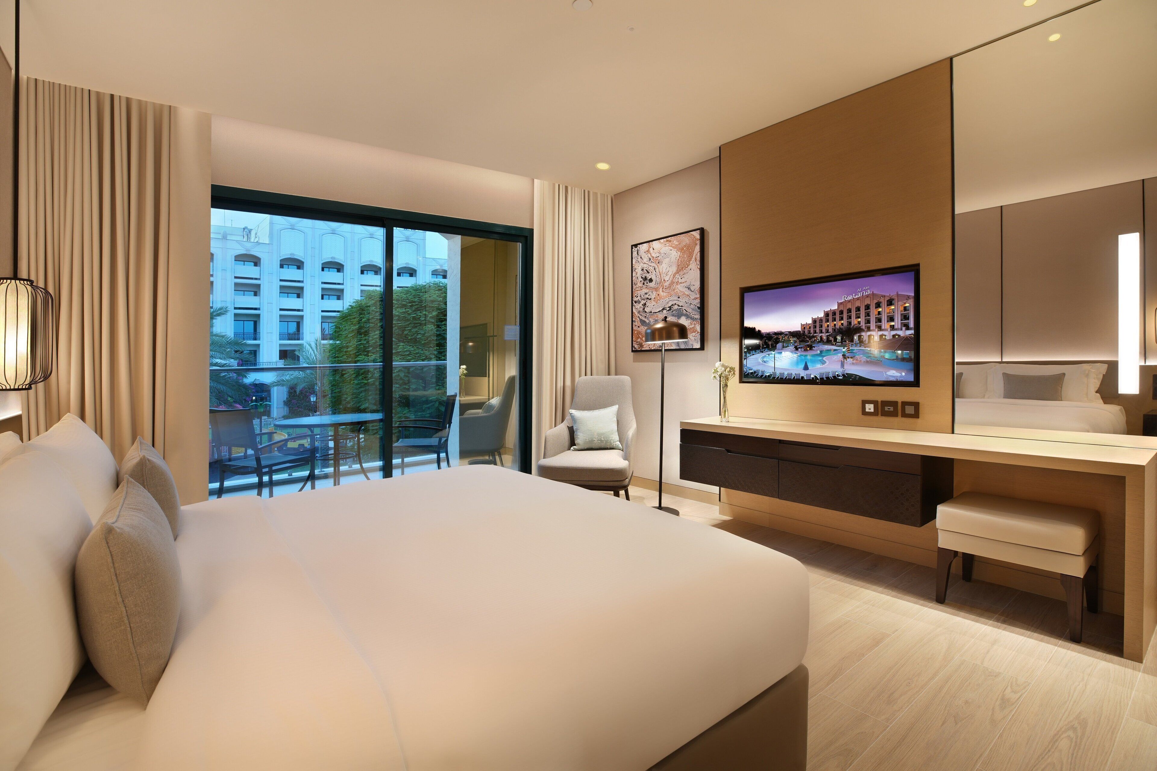 Quarto de hotel moderno com uma cama grande, uma escrivaninha, uma cadeira, uma televisão e uma varanda com vista para a cidade.