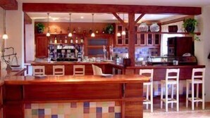 Uma cozinha com ilha central, banquetas, luminárias pendentes e armários de madeira.