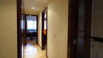 Um corredor com piso de madeira que leva a um quarto com cama e janela.