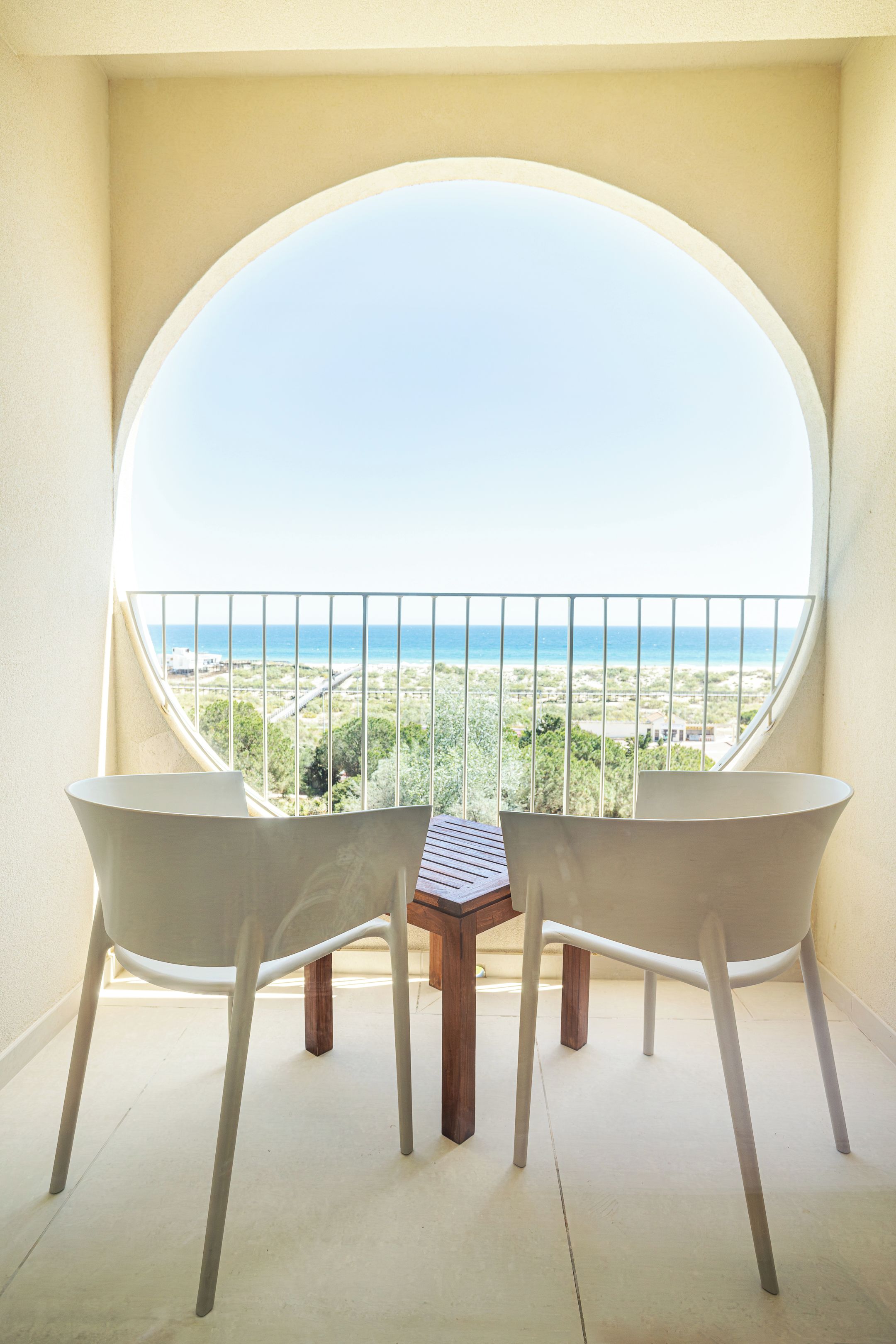 Varanda com mesa e cadeiras, vista para a praia e vegetação.