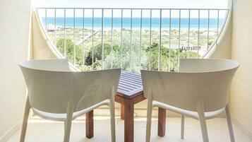 Varanda com mesa e cadeiras, vista para a praia e vegetação.