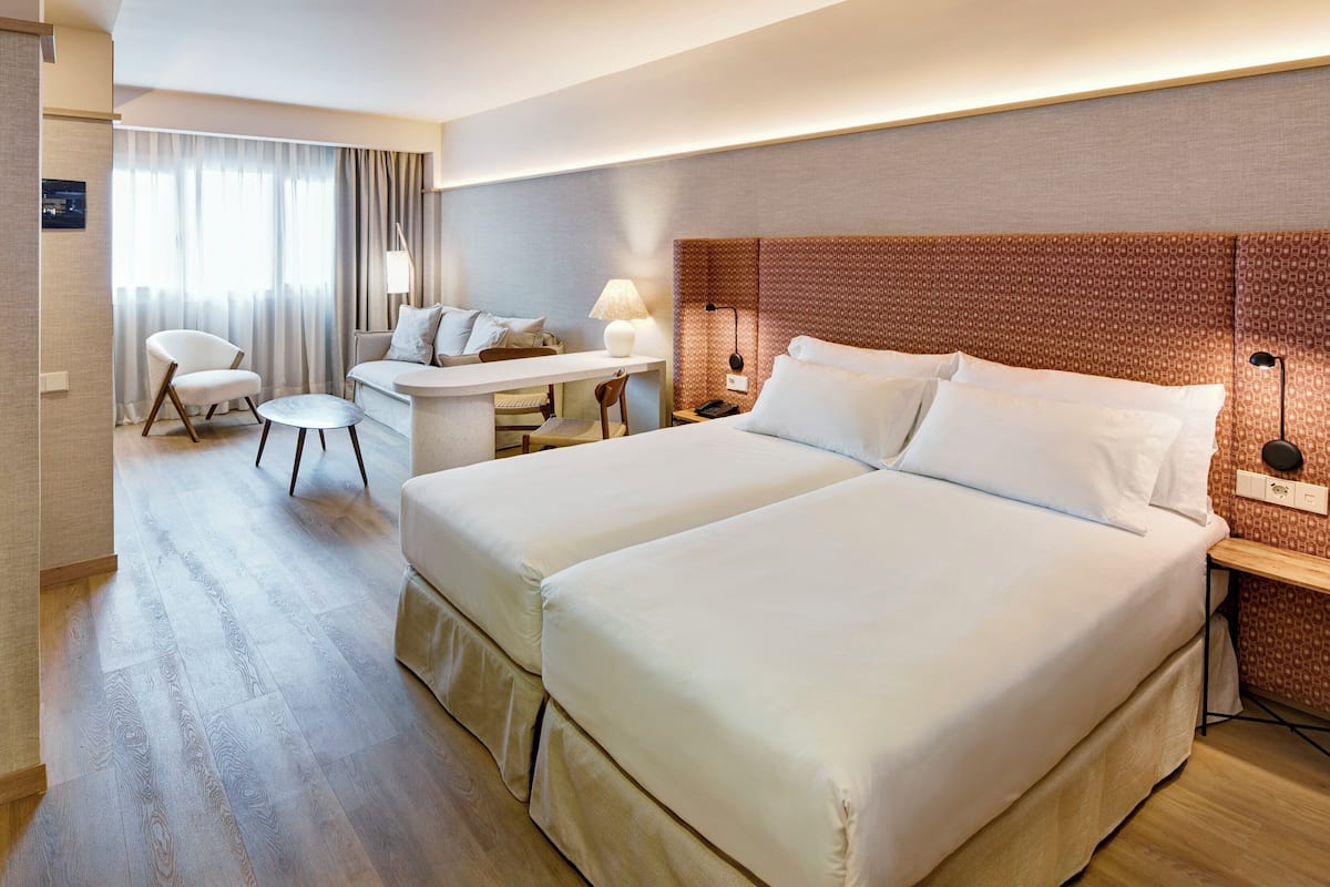 Quarto de hotel com cama, escrivaninha, cadeira e abajur.