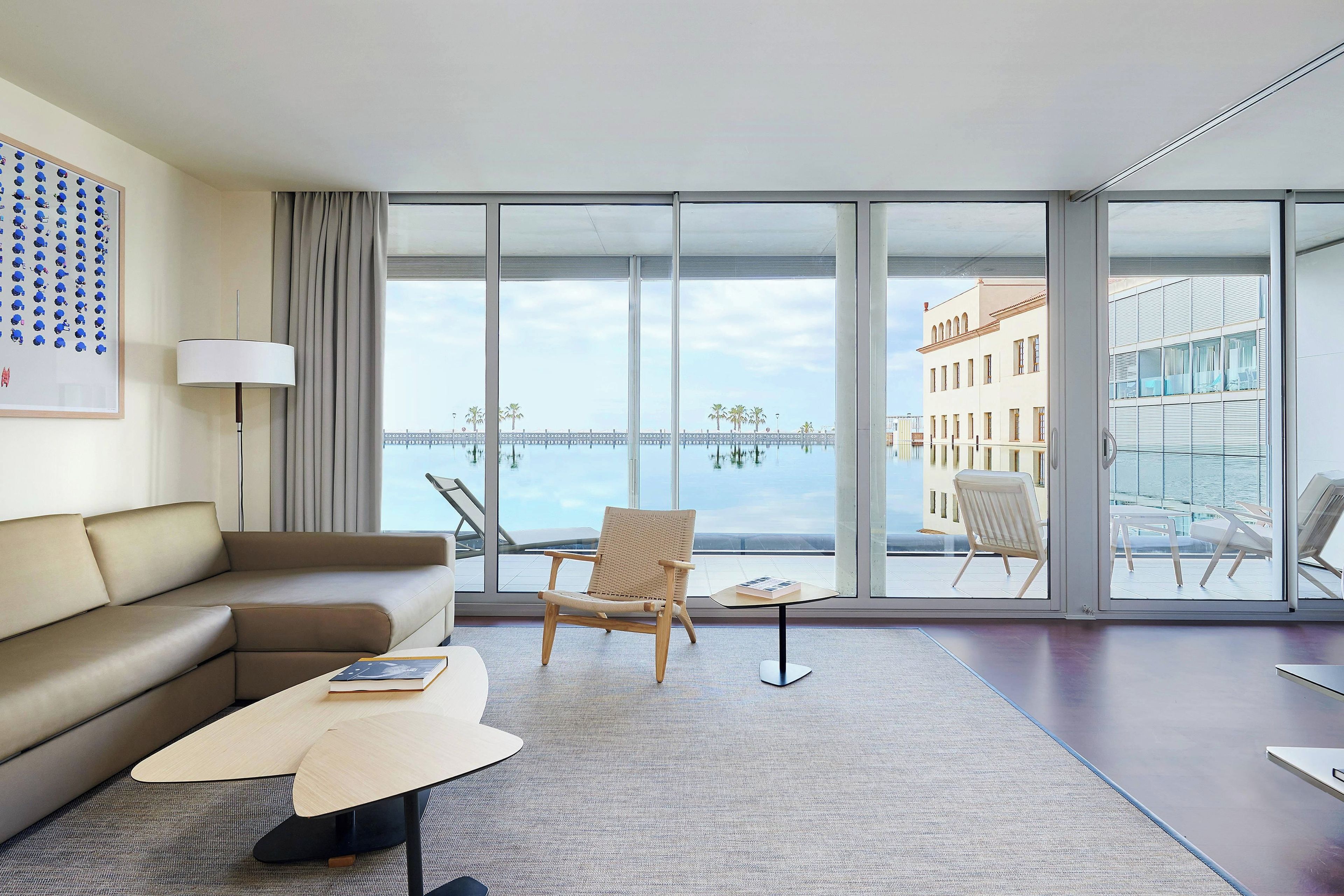 Quarto de hotel moderno com uma janela grande, um sofá, uma cadeira e uma mesa pequena.