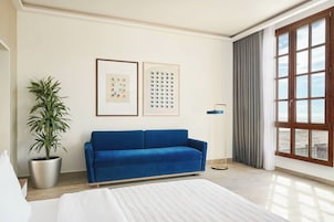 Quarto moderno com sofá azul, planta em vaso, cama e uma janela grande com vista.