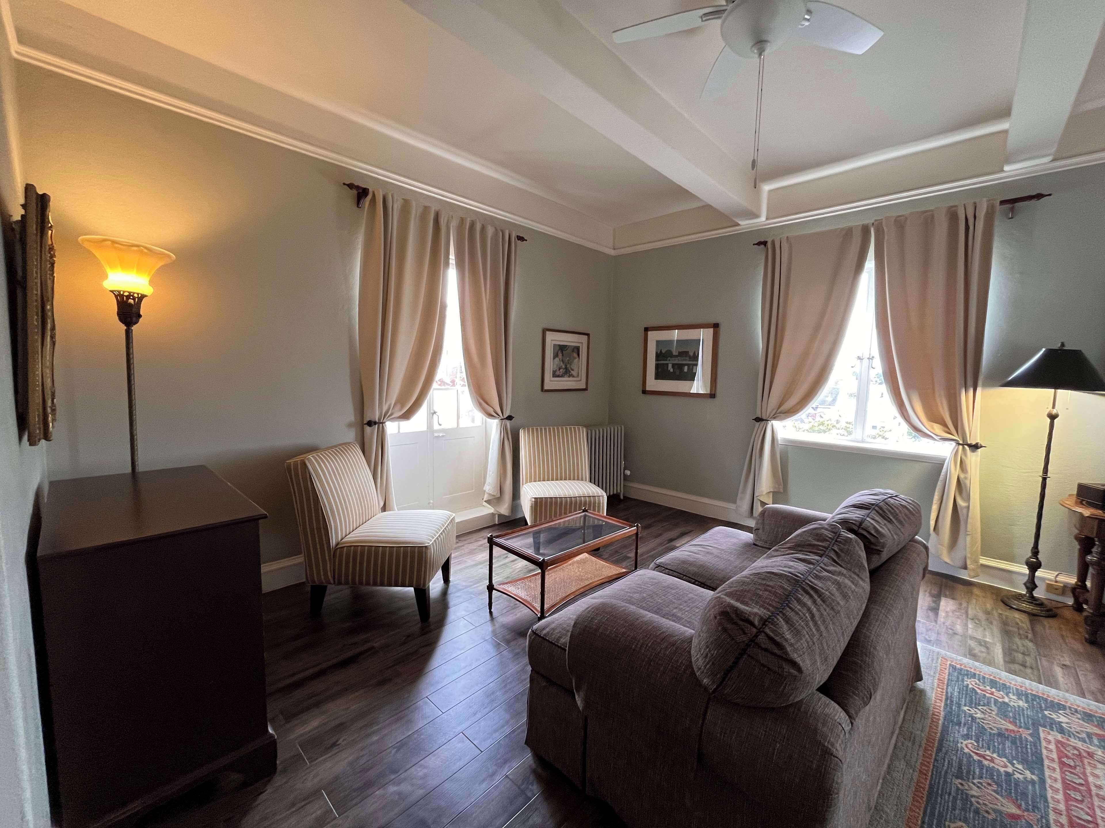 Uma sala de estar com sofá, poltronas, mesa de centro, abajur e radiador.