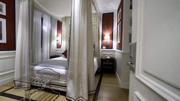 Quarto de hotel com cama, mesa de cabeceira, luminária e janela com cortinas.