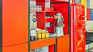 Uma cozinha com uma geladeira vermelha, prateleiras com potes e garrafas, e teto listrado.