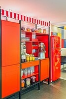 Uma cozinha com uma geladeira vermelha, prateleiras com potes e garrafas, e teto listrado.