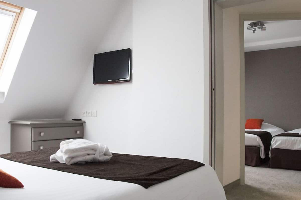 Quarto com cama, mesa de cabeceira, televisão de tela plana na parede e vista para um quarto adjacente com mais uma cama.