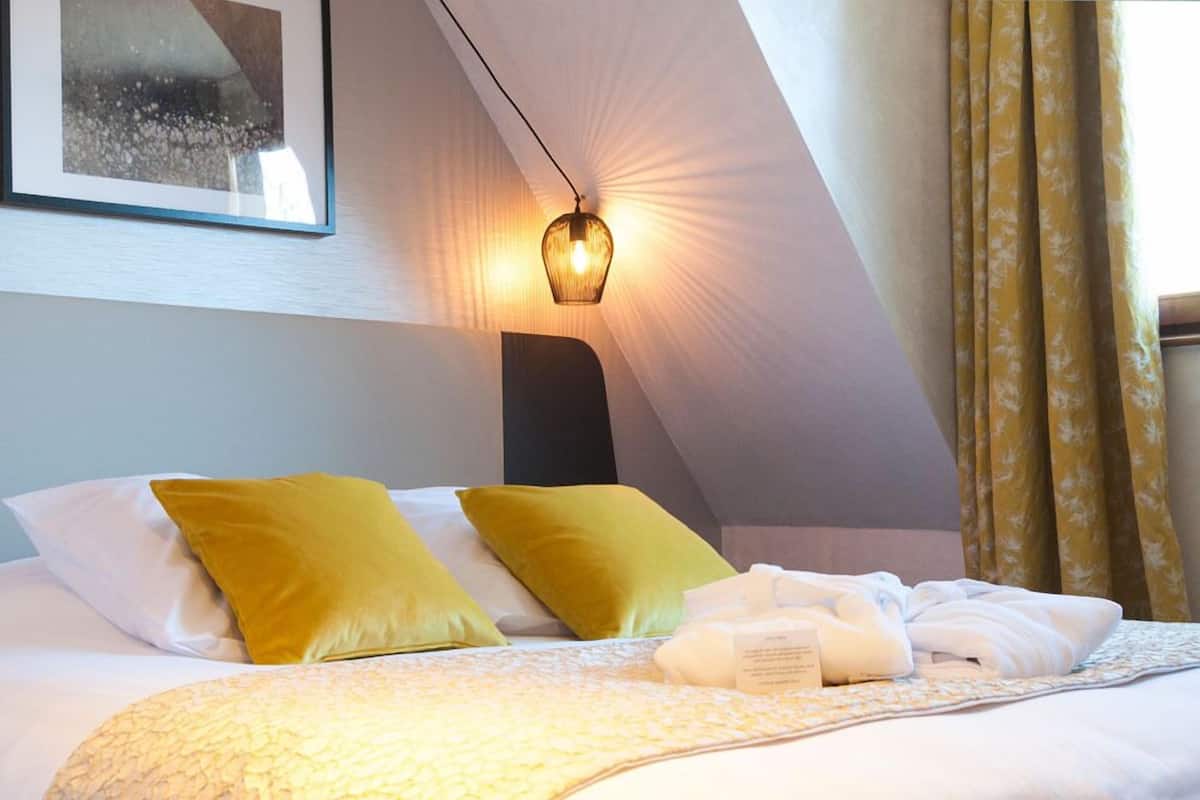 Quarto de hotel com uma cama, almofadas amarelas, abajur e um quadro na parede.