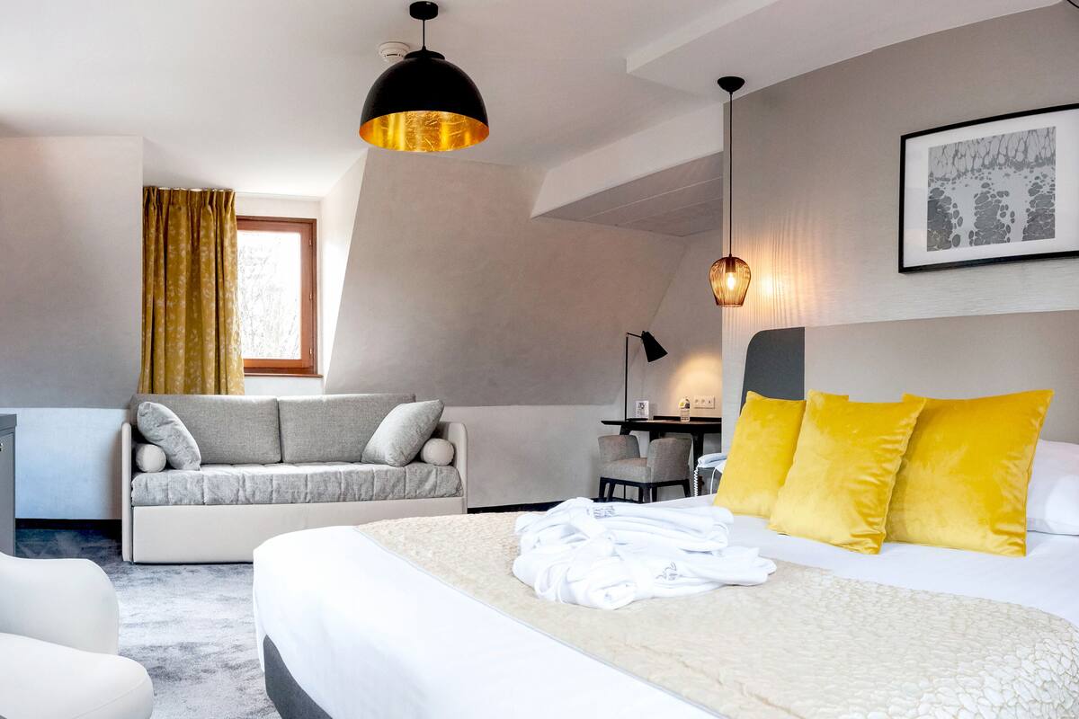 Quarto de hotel moderno com uma cama grande, um sofá, uma escrivaninha e uma cadeira.