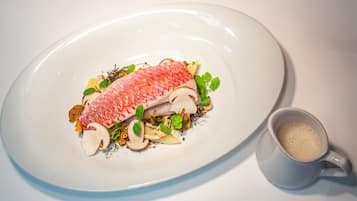 Um prato branco com peixe, cogumelos e ervas, e uma pequena chávena de café.