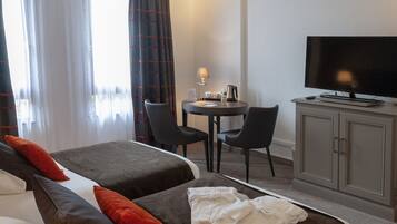 Quarto de hotel com duas camas, televisão, secretária com candeeiro e guarda-roupa.