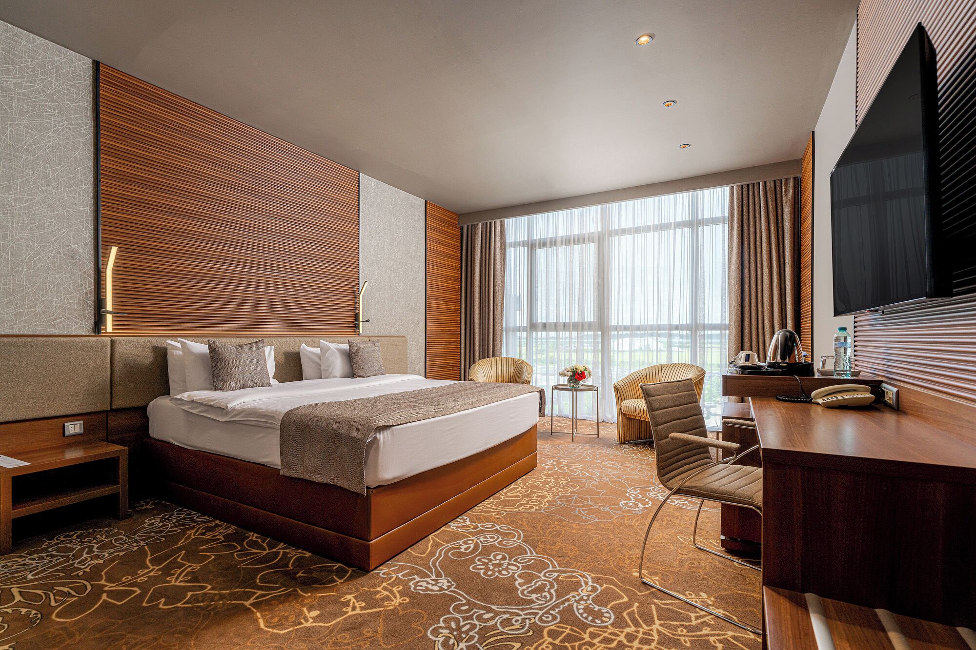 Quarto de hotel moderno com uma cama grande, uma mesa e uma televisão.