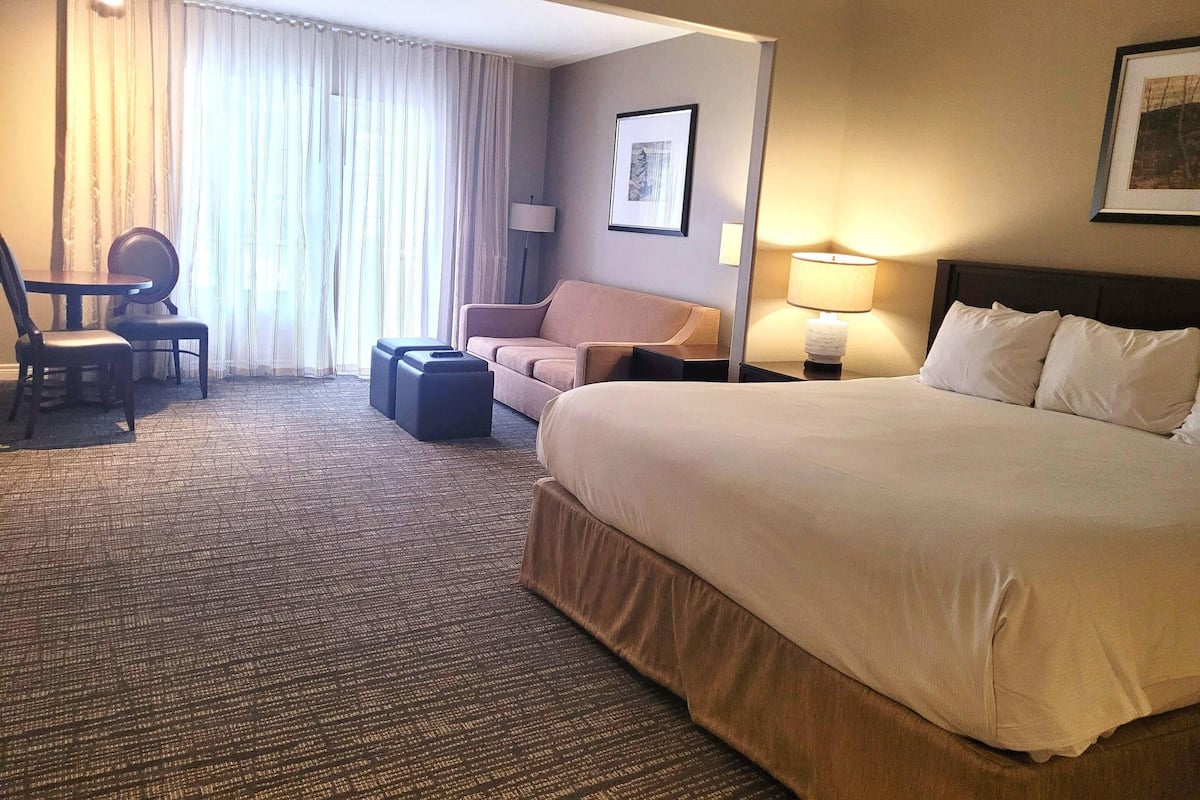 Quarto de hotel com uma cama grande, um sofá, uma cadeira, uma escrivaninha e um abajur.