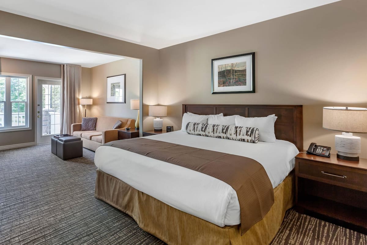 Quarto de hotel com cama grande, sofá, escrivaninha e luminária.