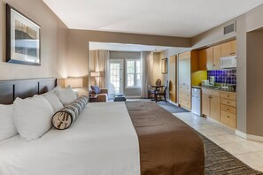 Quarto de hotel com uma cama grande, uma mesa, uma cadeira e uma kitchenette.