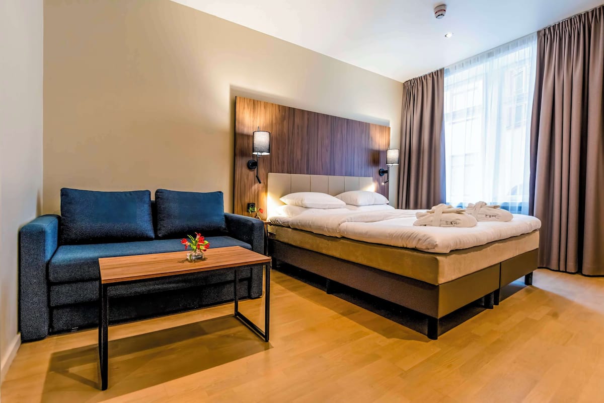 Quarto de hotel com cama, sofá, mesinha e criado-mudo.
