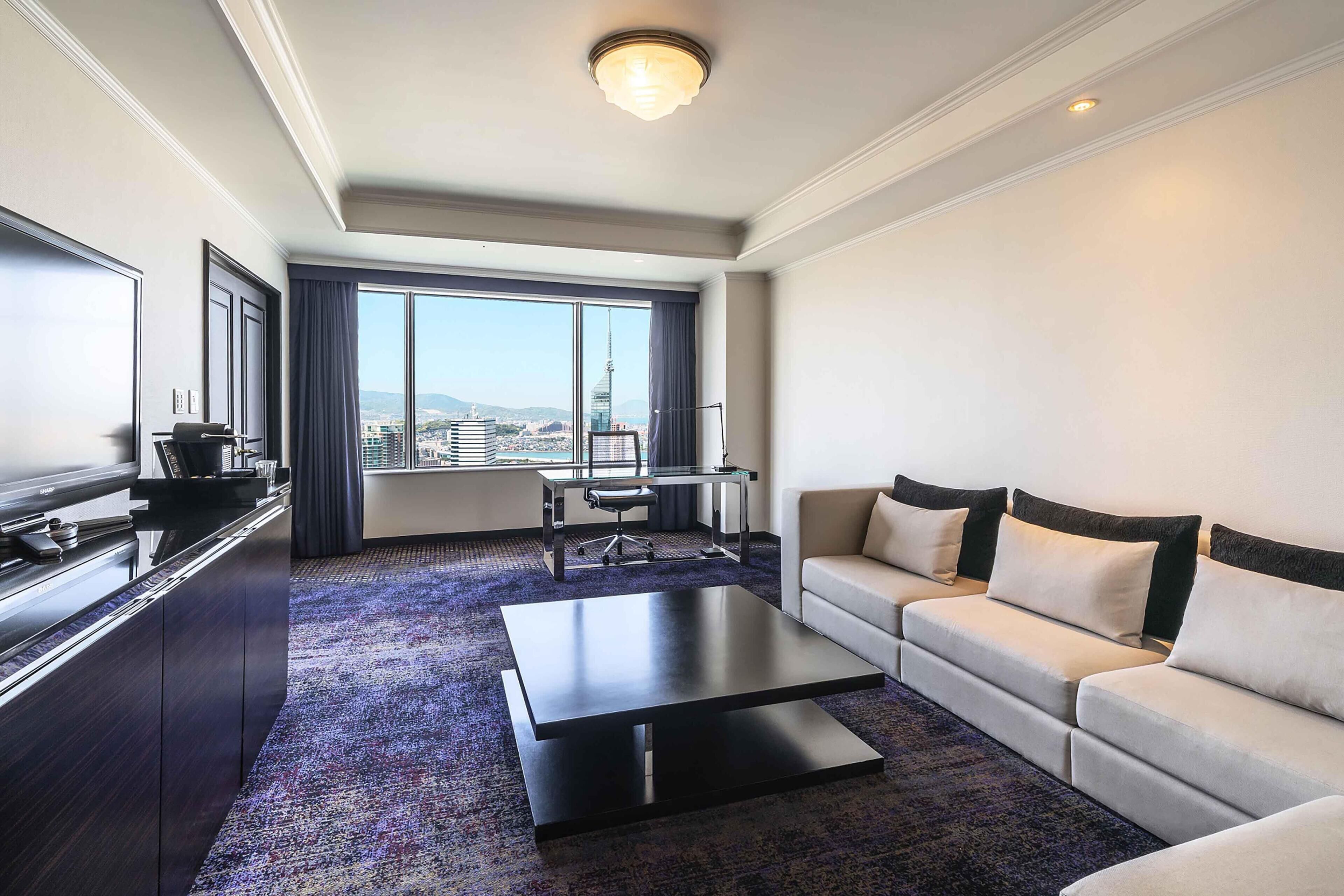 Quarto de hotel moderno com uma grande janela, um sofá, uma mesa de centro e uma escrivaninha.