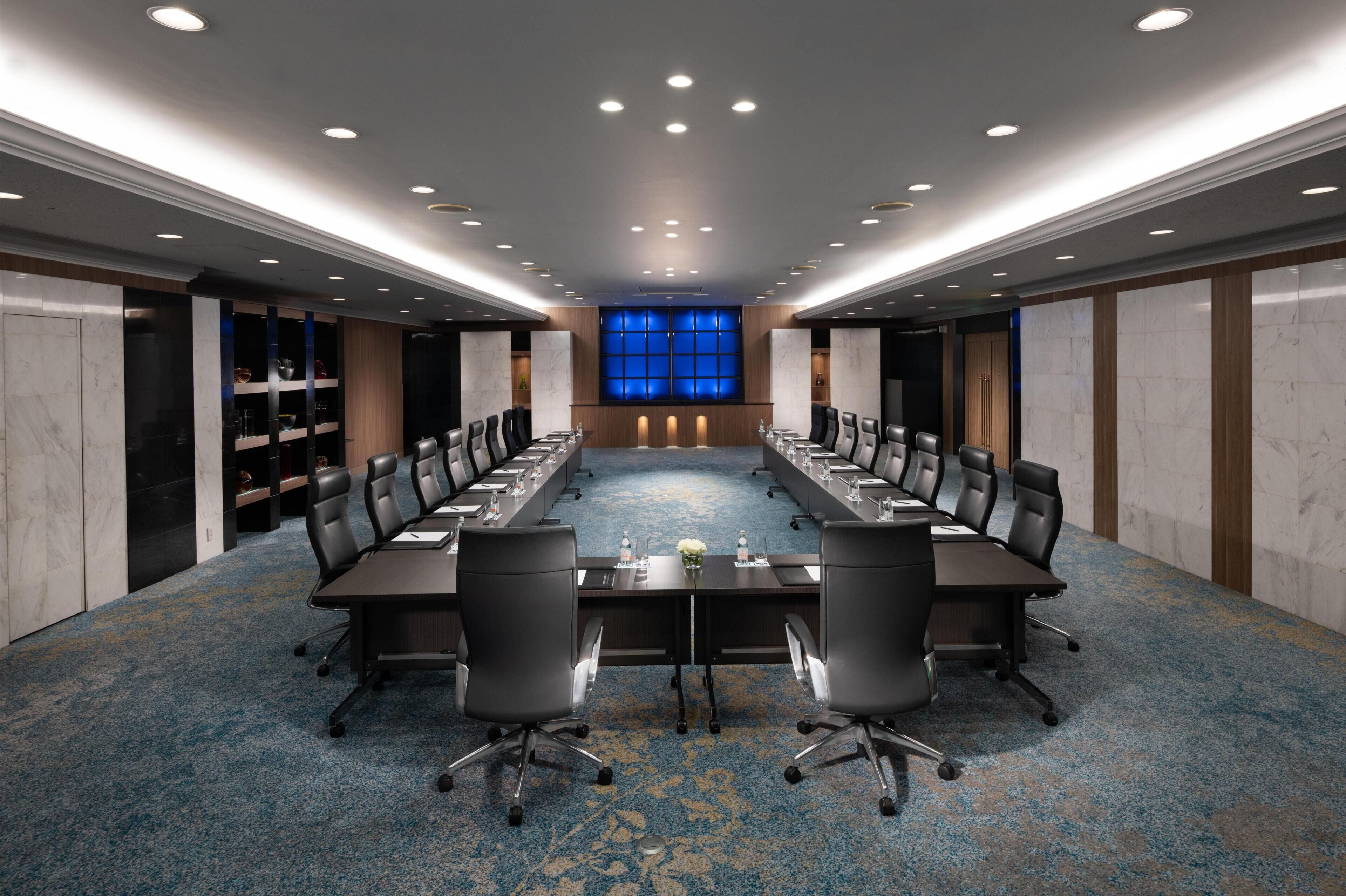 Uma sala de conferência com uma mesa comprida, cadeiras e um tapete azul.