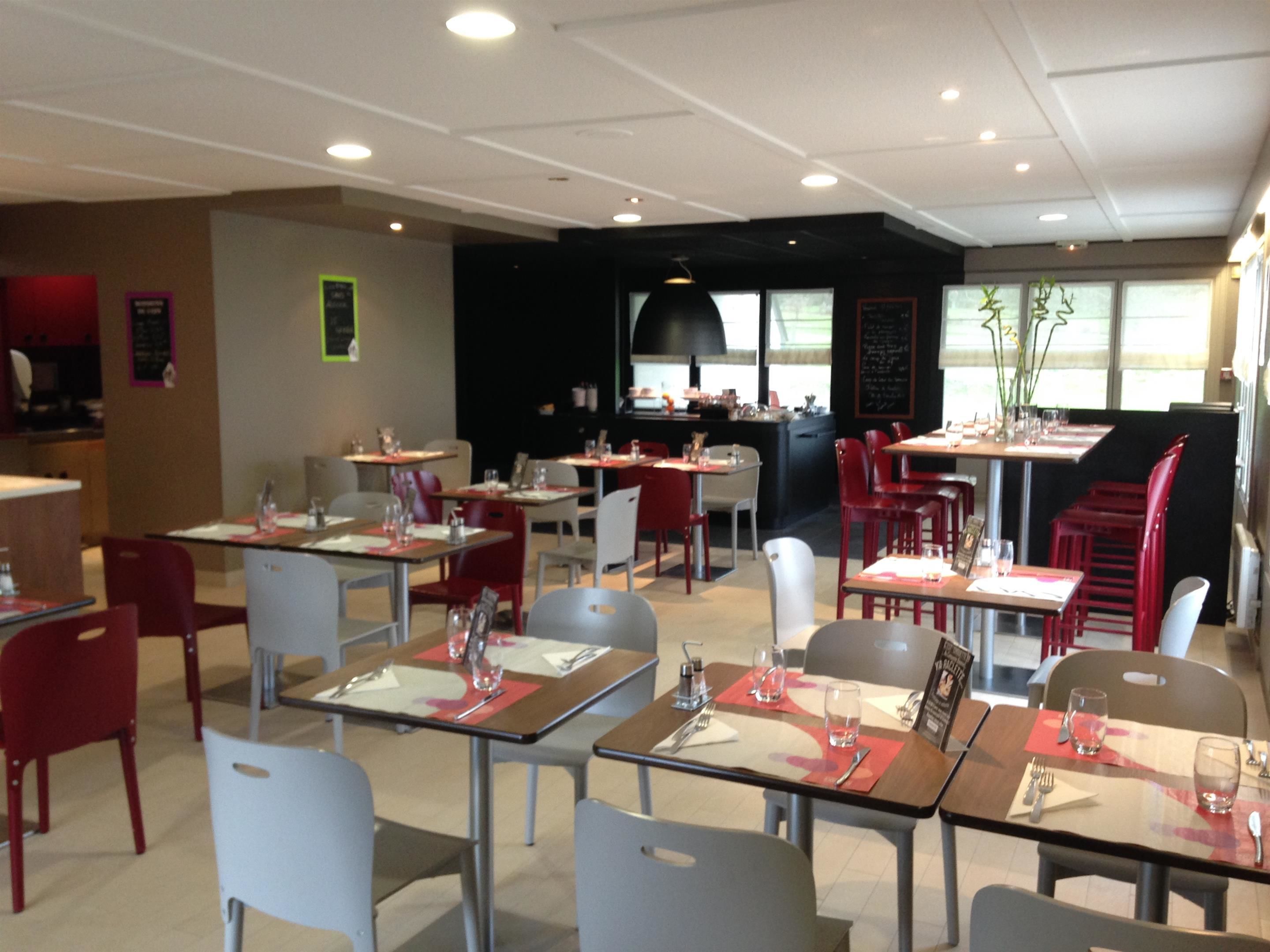 Um restaurante com várias mesas e cadeiras, algumas com estofamento vermelho e outras cinzento.