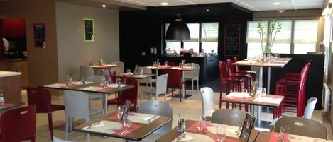 Um restaurante com várias mesas e cadeiras, algumas com estofamento vermelho e outras cinzento.