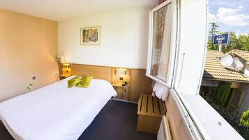 Quarto de hotel com cama, mesa de cabeceira, abajur e janela com vista para o exterior.