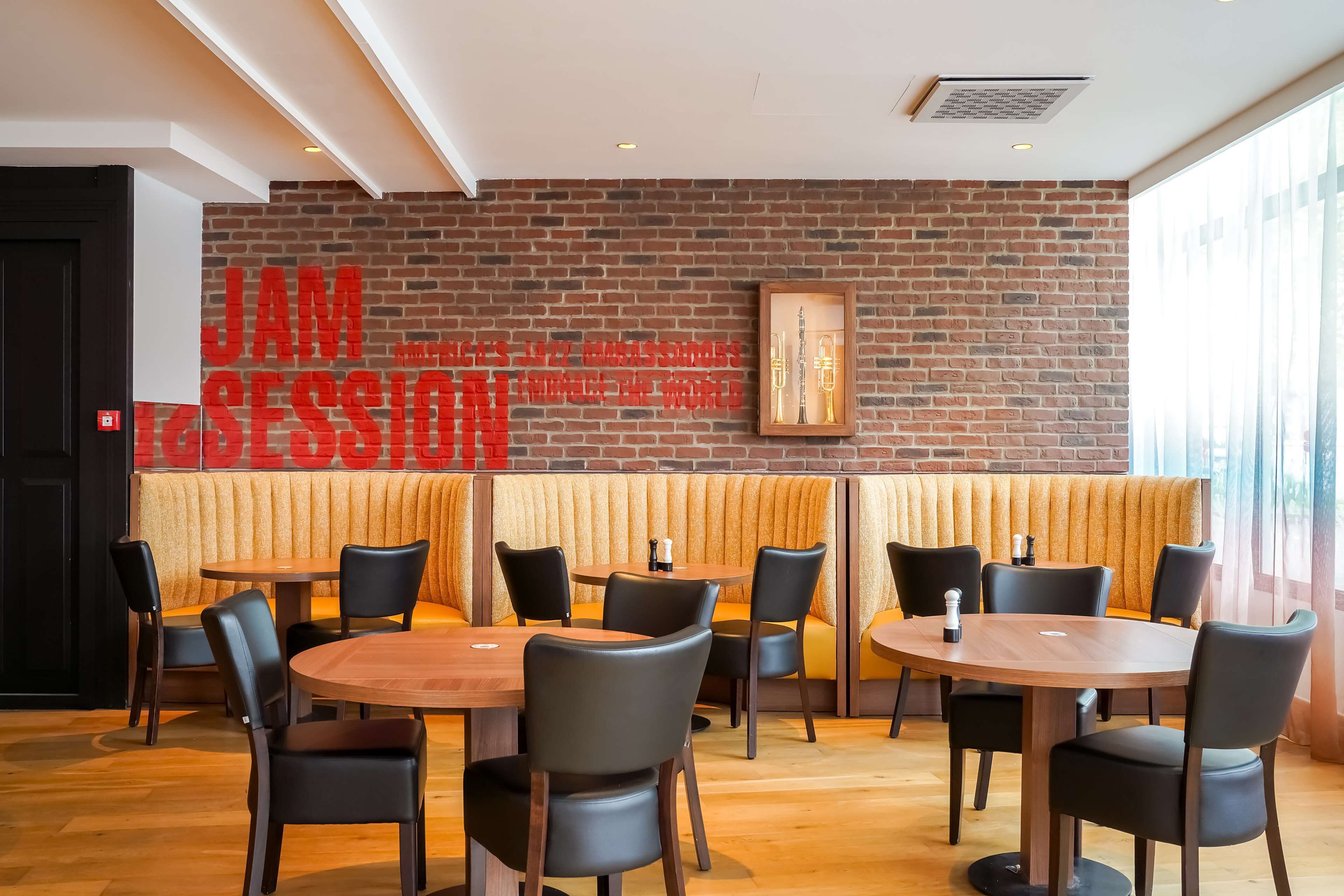 Interior de restaurante com paredes de tijolo, mesas de madeira e cadeiras pretas.