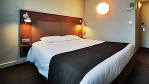 Quarto de hotel com uma cama grande, duas luminárias de cabeceira, uma luminária redonda na parede e um painel de cabeceira de madeira.