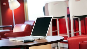 Um laptop sobre uma mesa, com uma cadeira vermelha ao fundo.